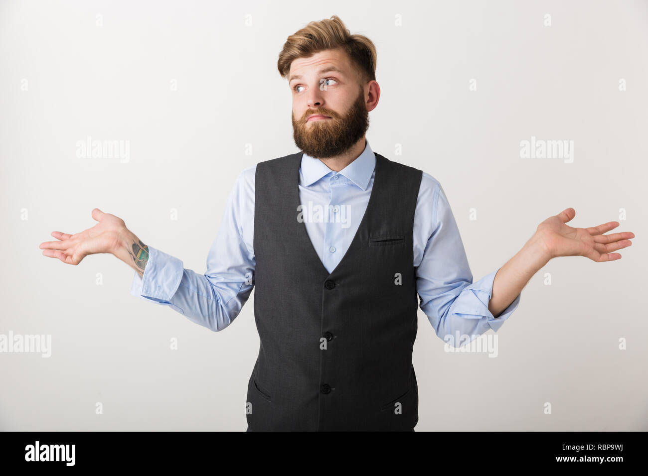 Image of a confused young bearded man standing isolated over white wall ...