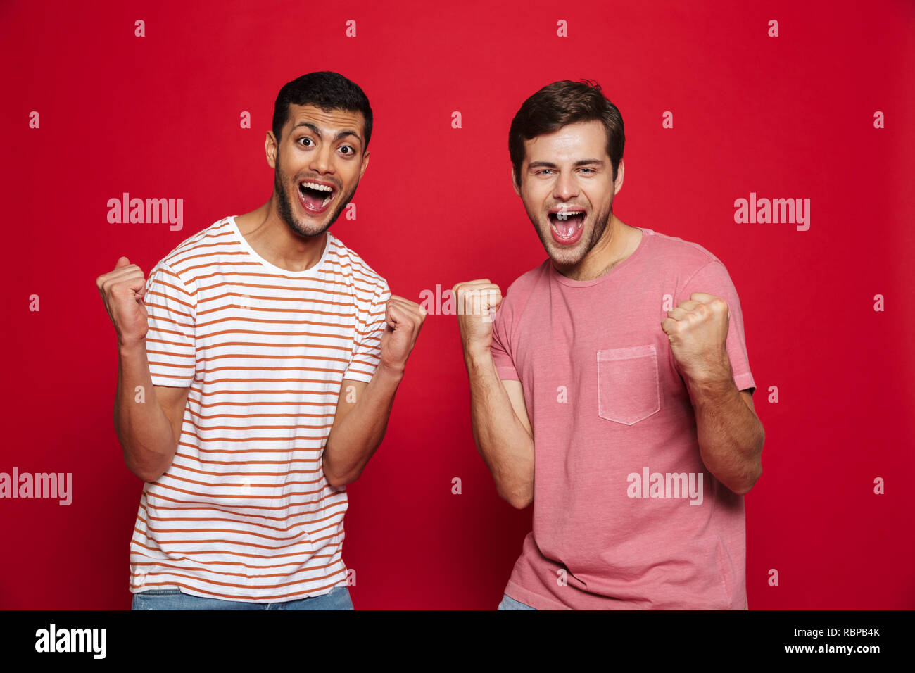 Two cheerful young men standing isolated over red background ...