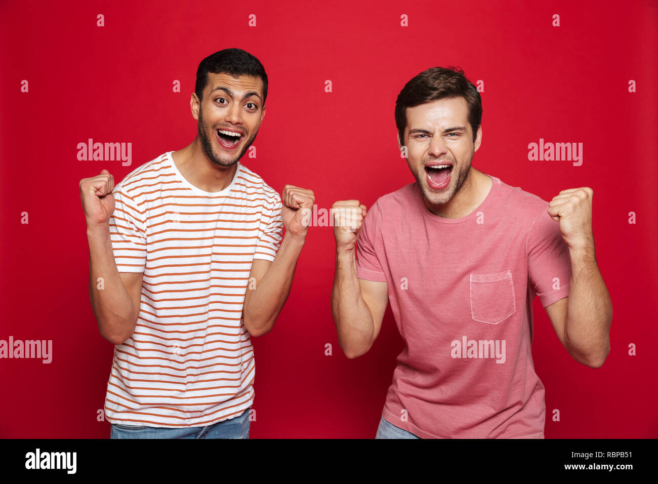 Two cheerful young men standing isolated over red background ...