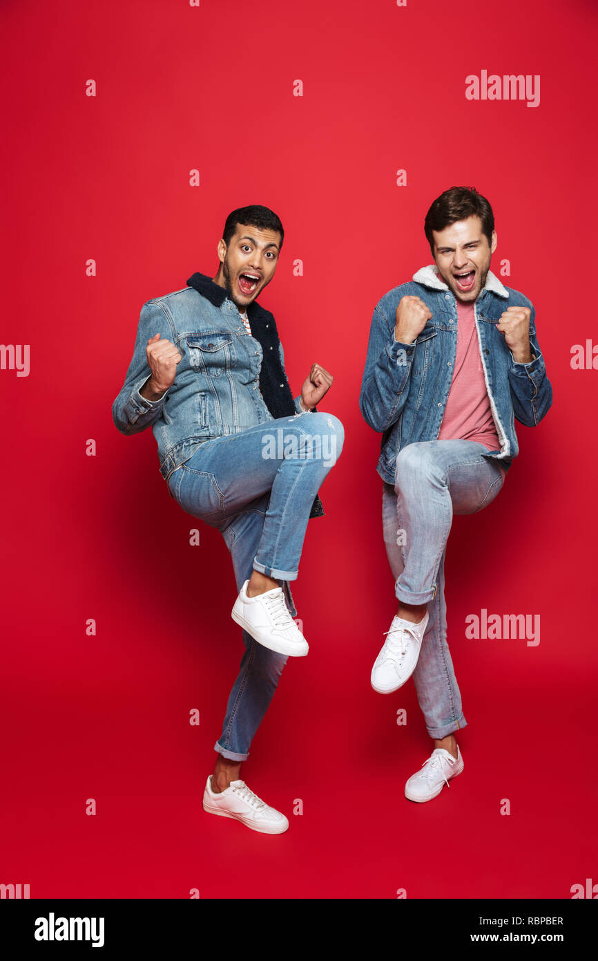 Full length of two cheerful young men jumping isolated over red ...