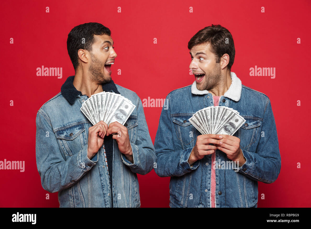 Two cheerful young men standing isolated over red background, holding ...