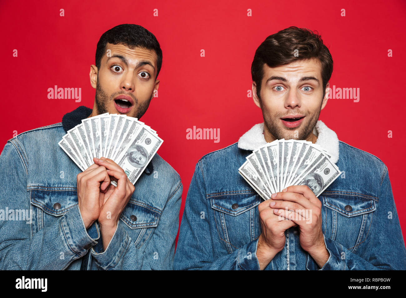 Two cheerful young men standing isolated over red background, holding ...