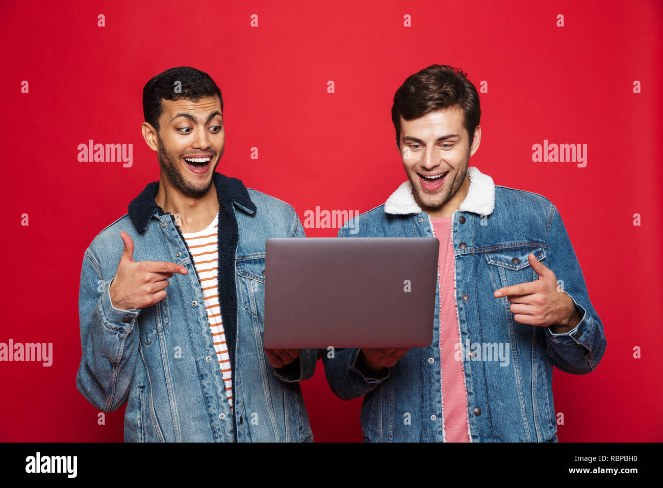 Two cheerful young men standing isolated over red background, holding ...