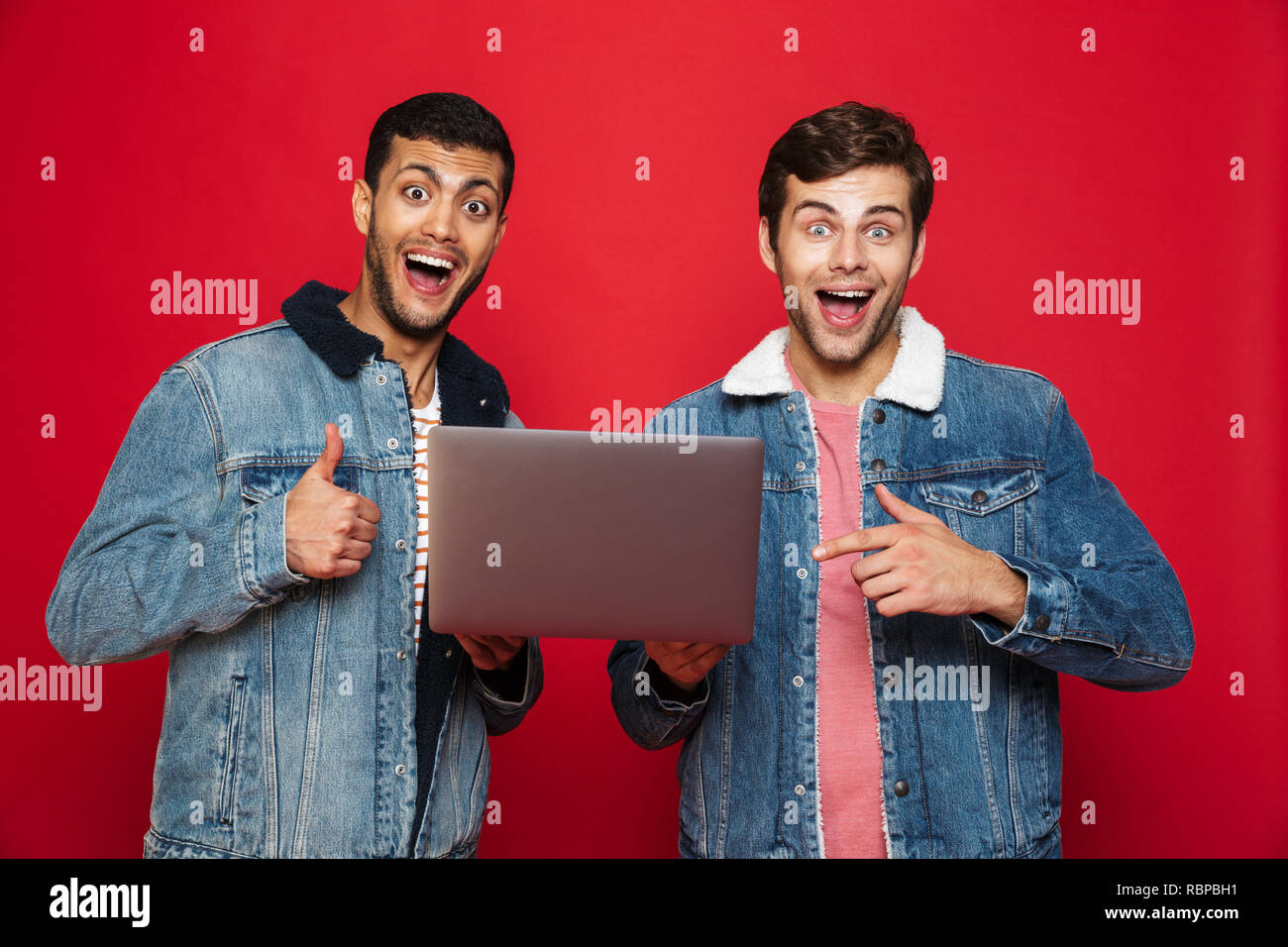 Two cheerful young men standing isolated over red background, holding ...