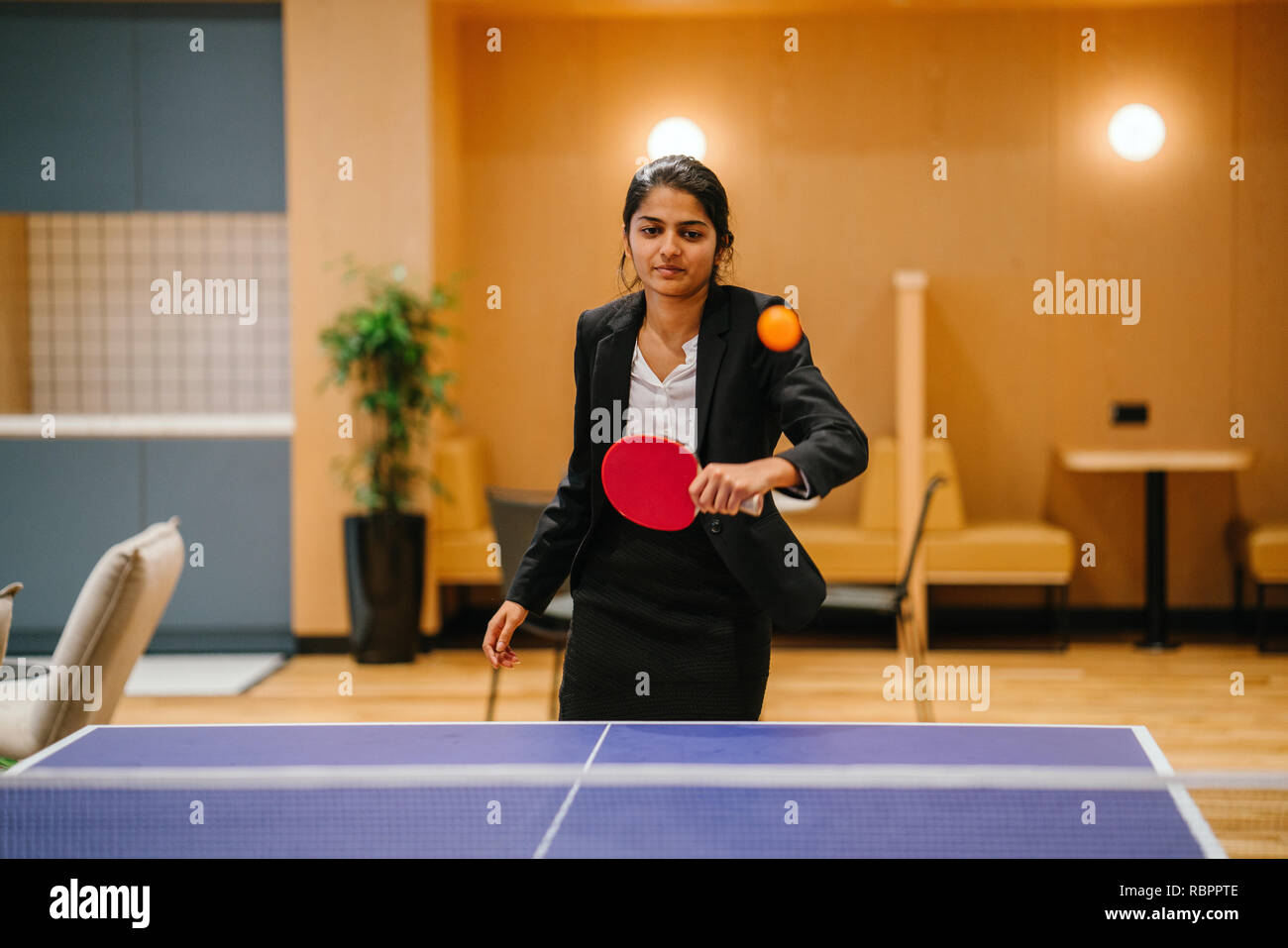A young Indian Asian woman in a suit smiles and laughs as she plays ...