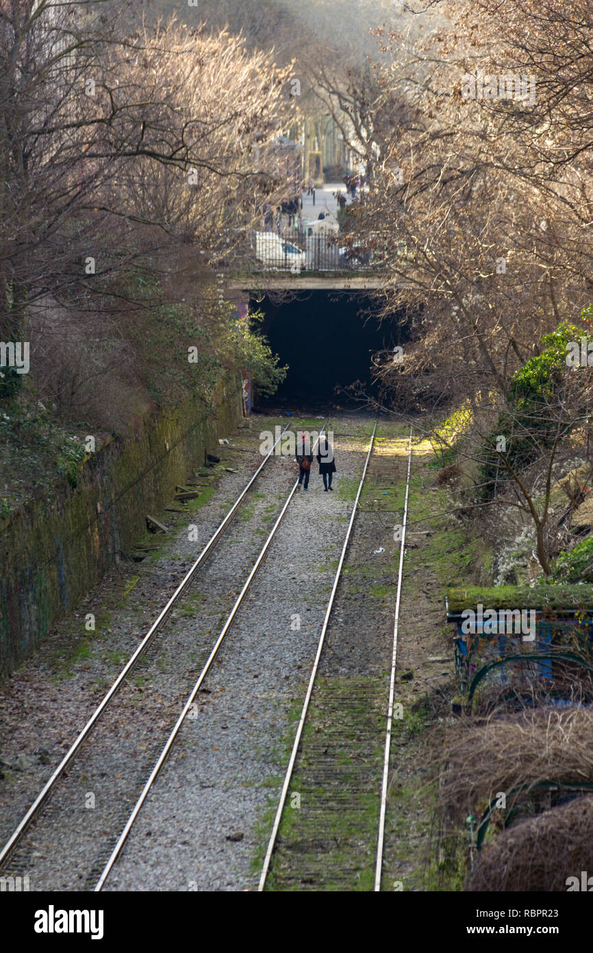A couple walks along tree lined railroad tracks toward a tunnel Stock ...