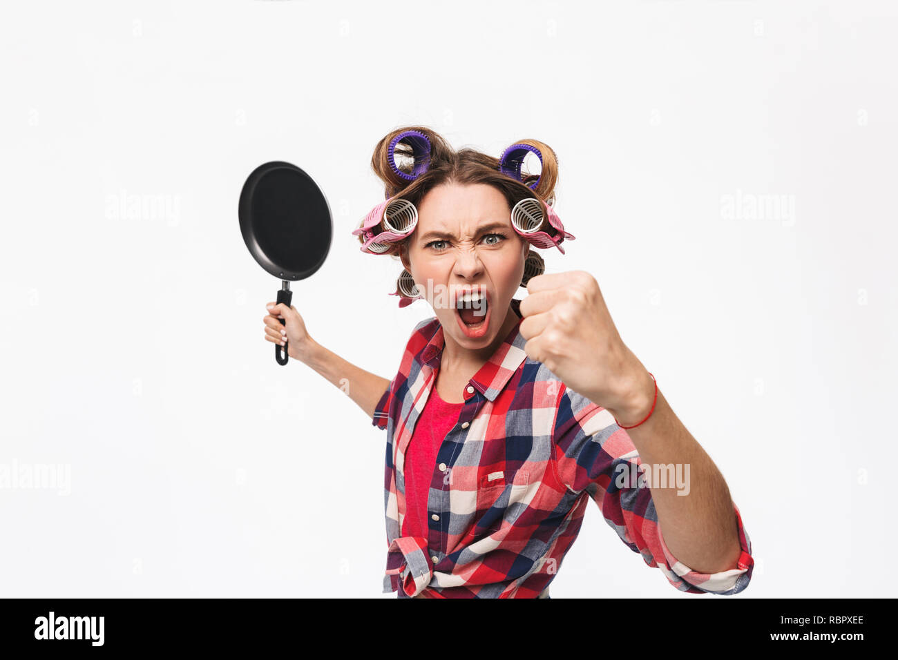 Angry housewife with curlers in hair standing isolated over white ...