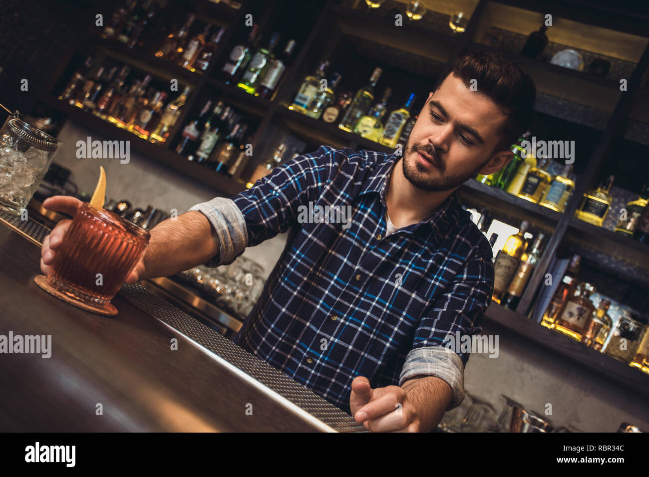 Young barman standing at bar counter serving cocktail concentrated ...