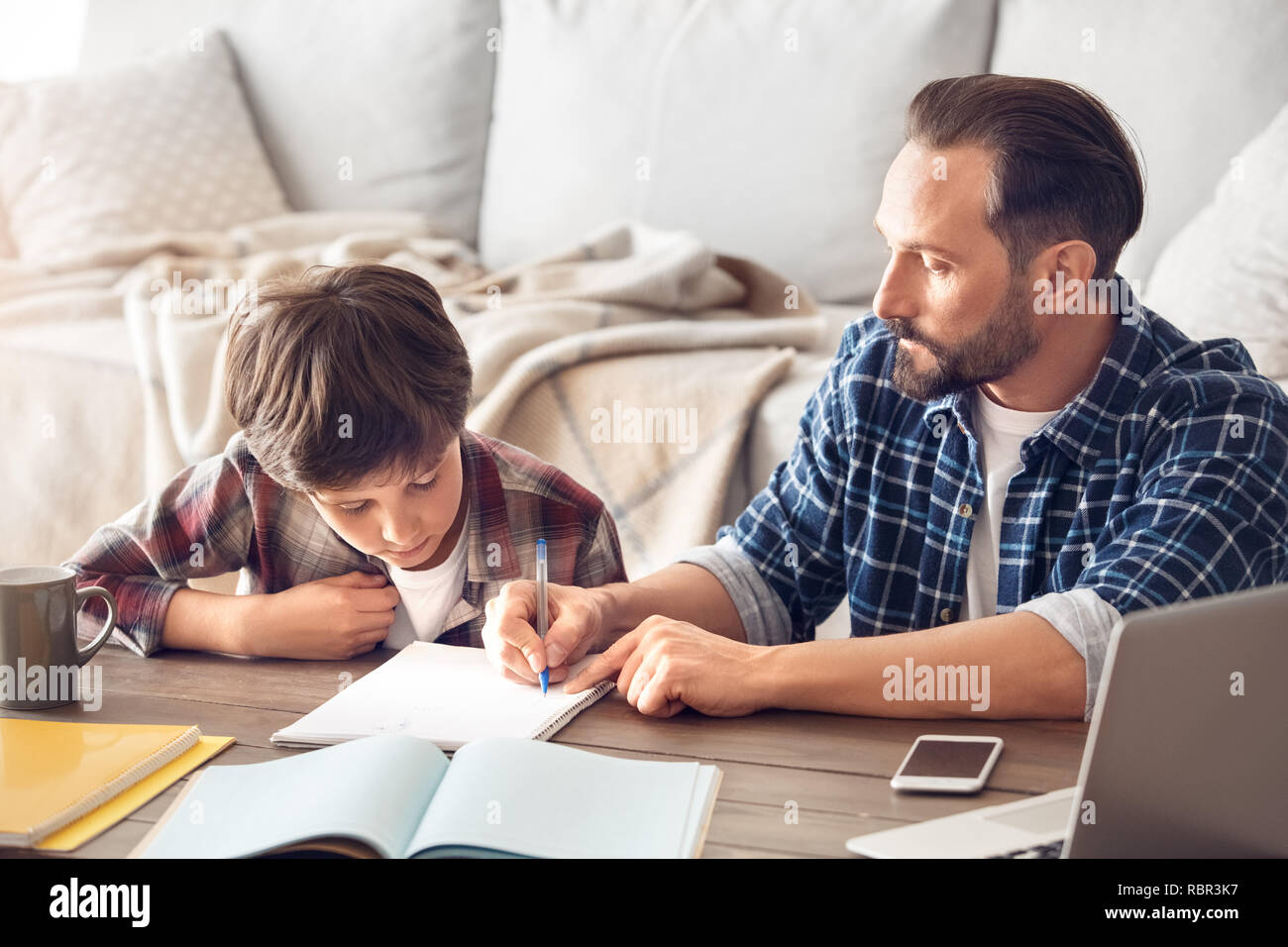Father and little son together at home sitting at table dad showing son ...
