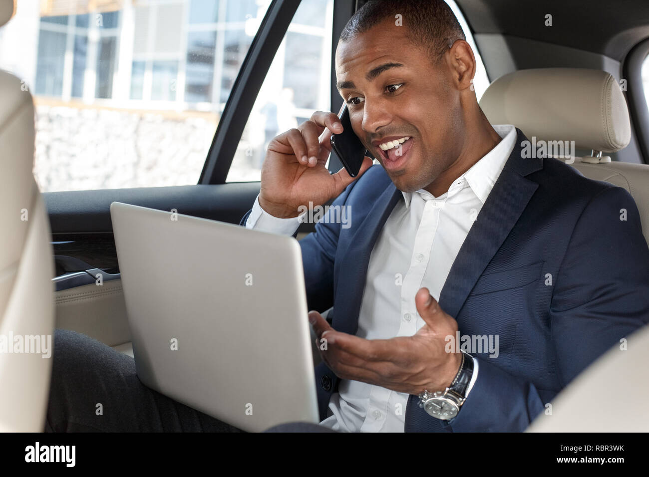 Young mulatto businessman sitting on the back seat in the car talking ...