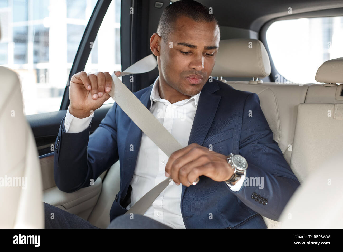 Young mulatto businessman sitting on the back seat in the car fastening ...