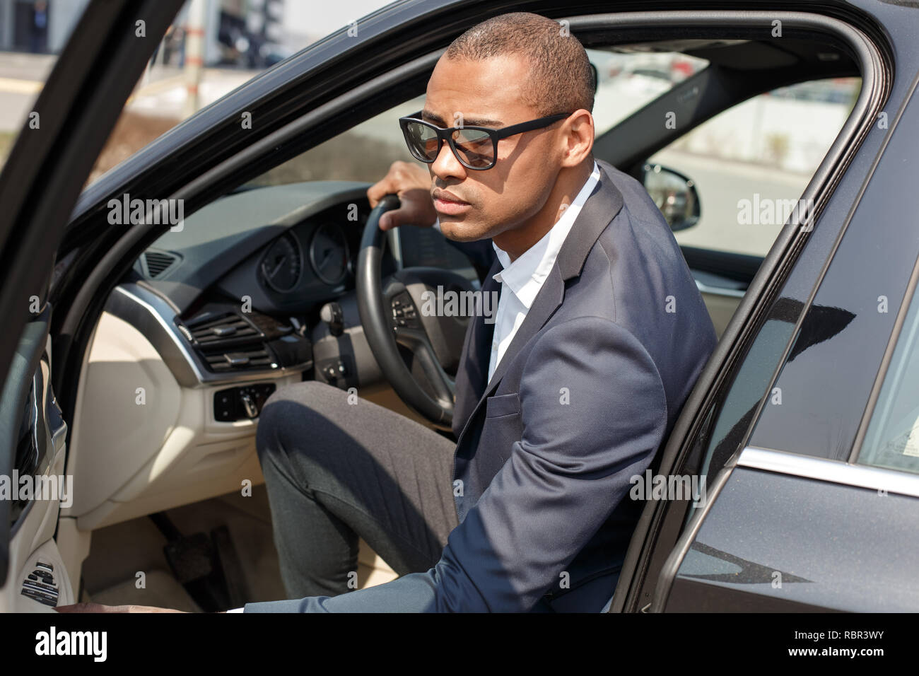 Young mulatto businessman wearing sunglasses sitting in the car door ...