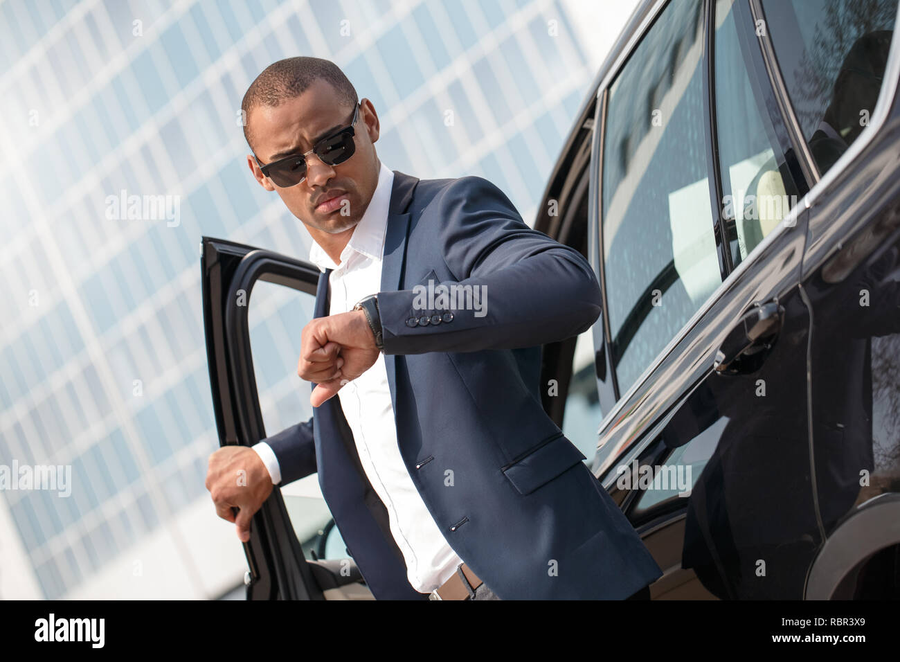 Young mulatto businessman wearing sunglasses standing near car holding ...