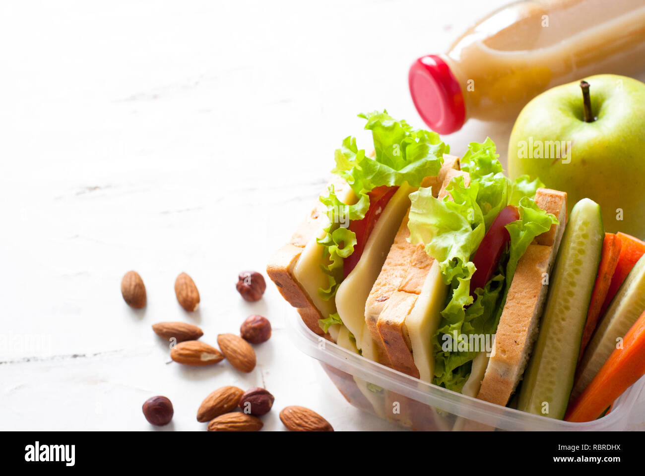 Lunch box with sandwich, vegetables, juice, nuts and apple on white ...