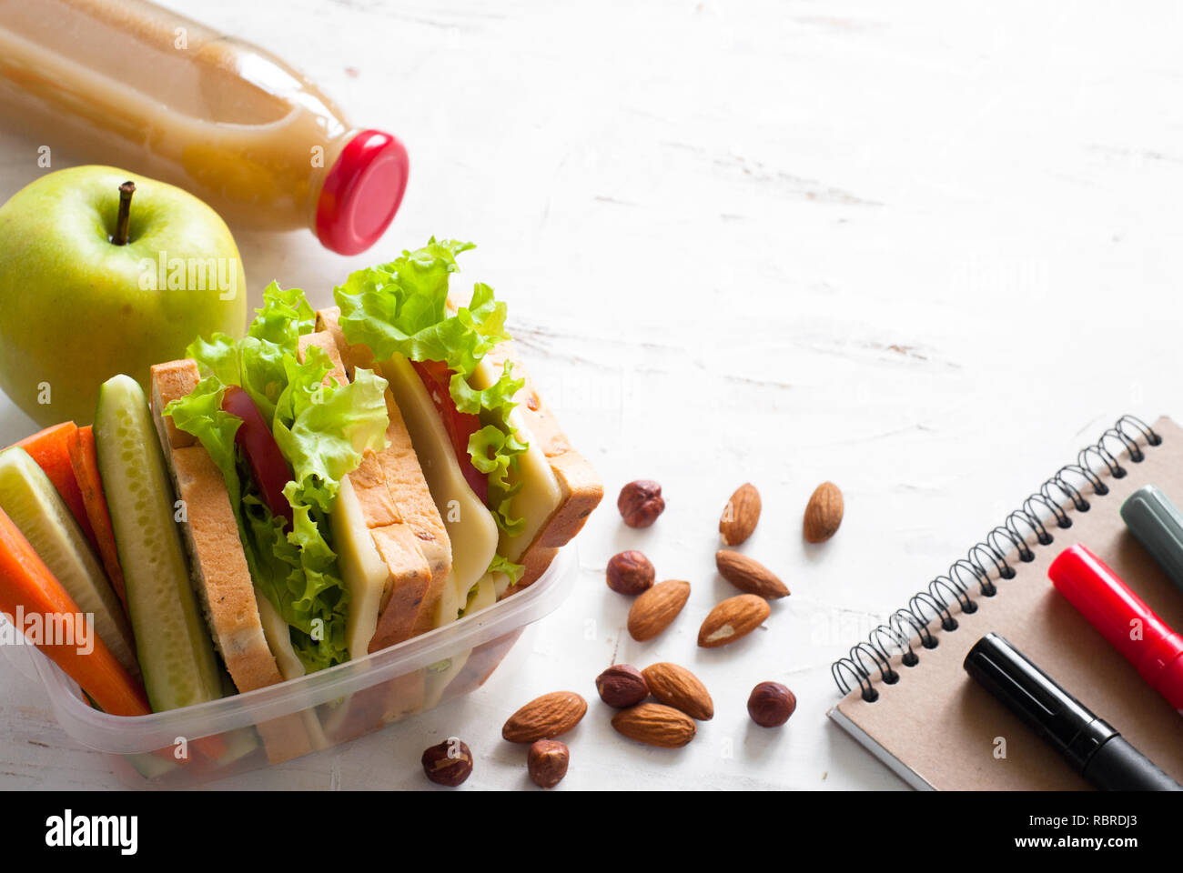 Lunch box with sandwich, vegetables, juice, nuts and apple on white ...