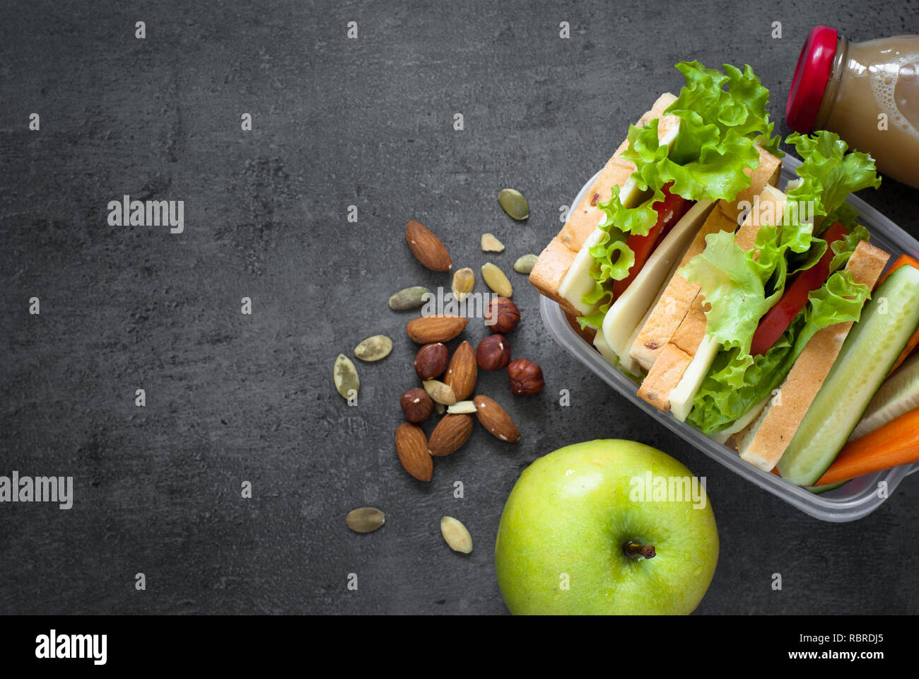 Lunch box with sandwich, vegetables, juice, nuts and apple on black ...