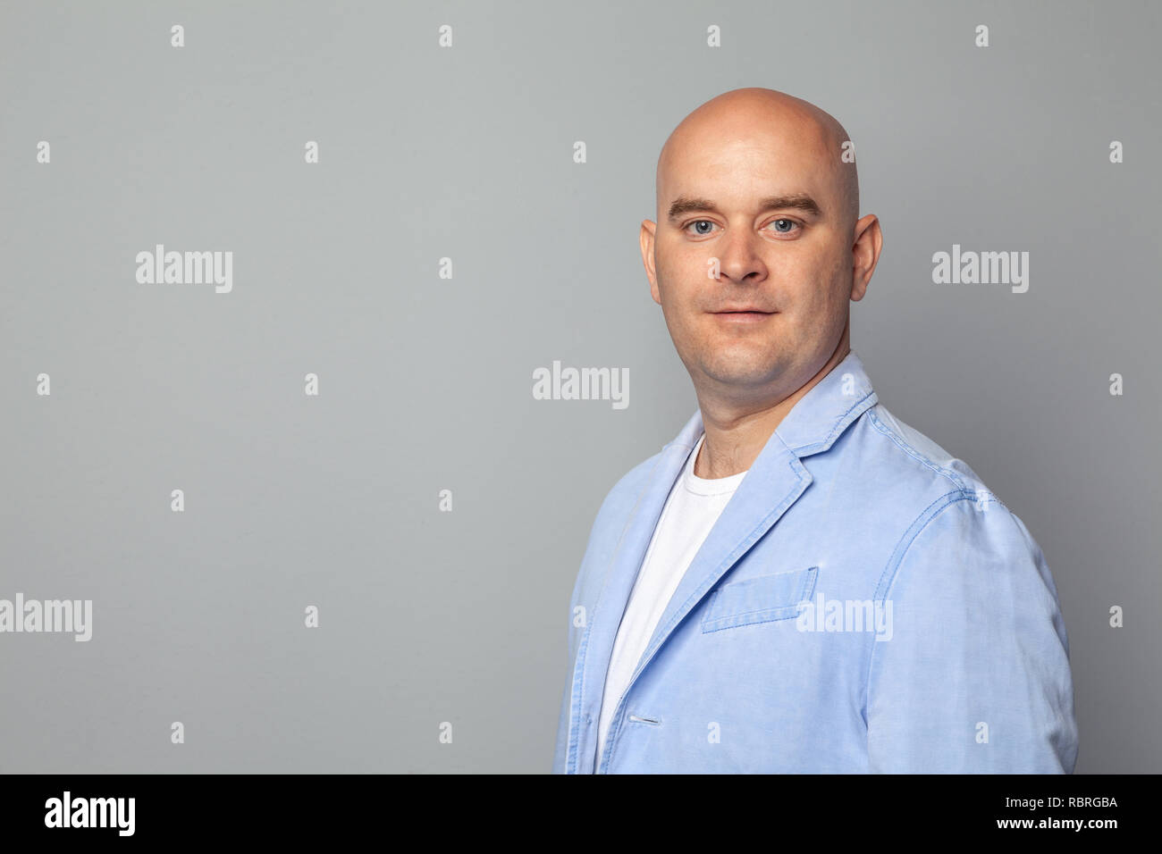 bald man in a blue jacket against a gray wall Stock Photo - Alamy