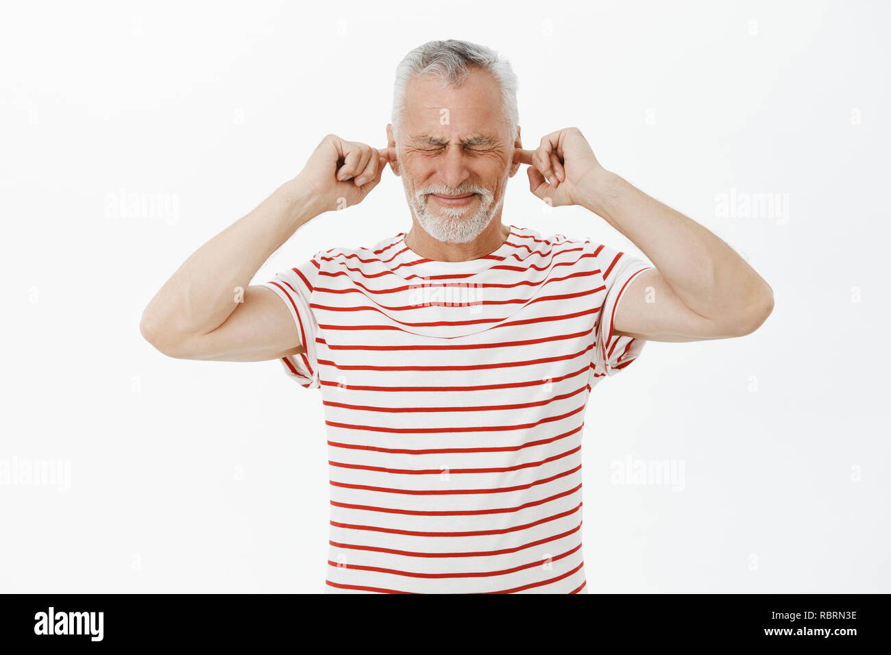 Man closes ears and eyes with intense irritated expression hearing loud ...