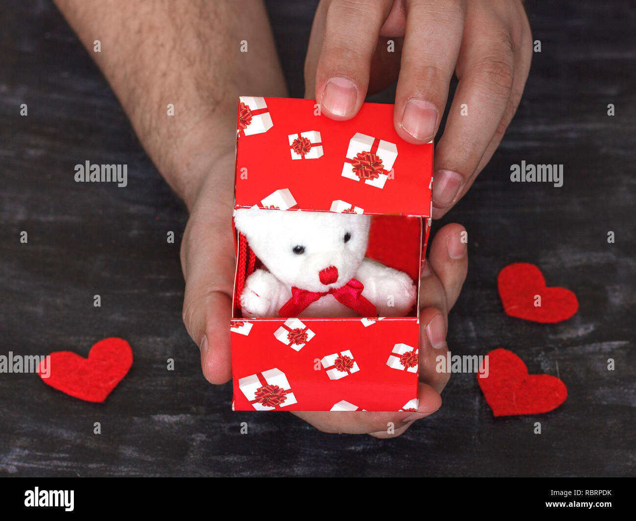 A man makes a proposal. Teddy bear in a red box with hearts as a gift ...
