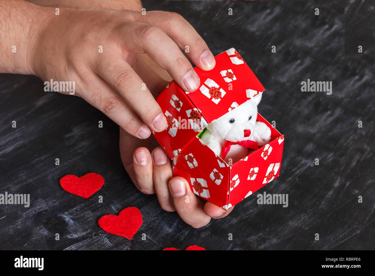 A man makes a proposal. Teddy bear in a red box with hearts as a gift ...