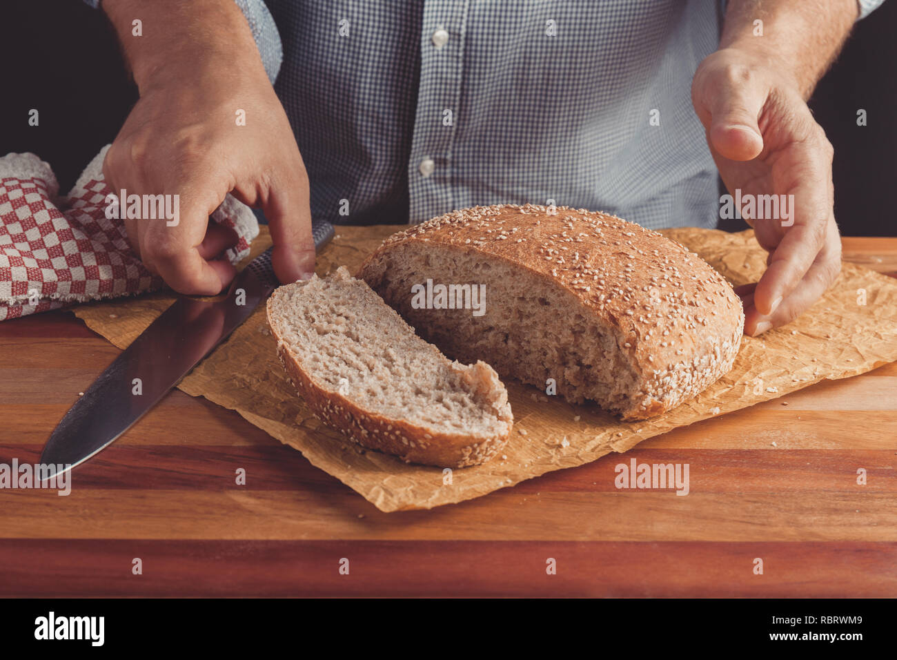 A man cuts freshly baked whole-wheat bran bread with a sharp knife ...