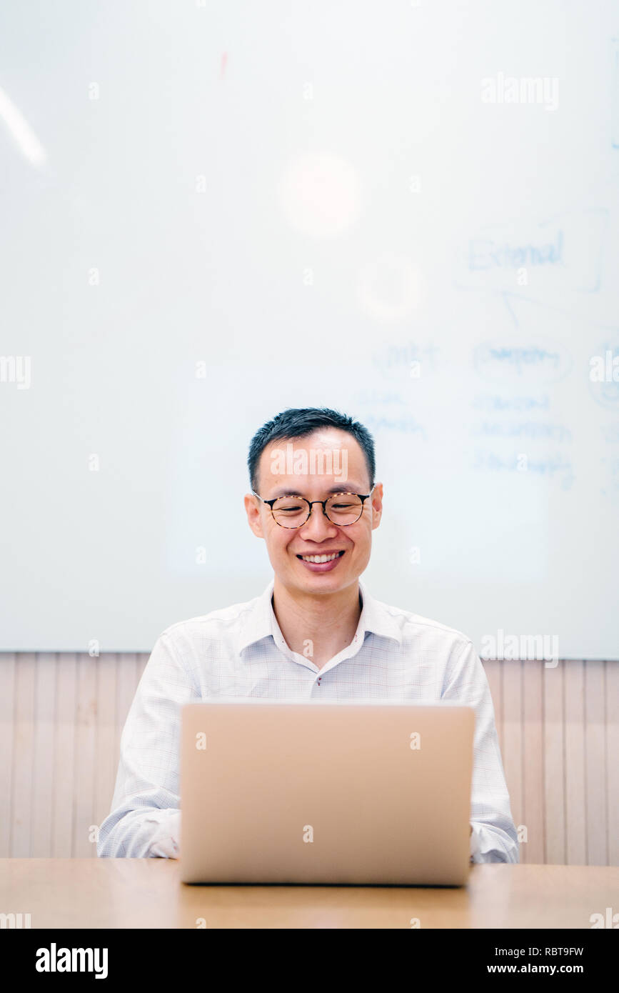 A young Chinese Asian business man is working on his laptop computer in ...