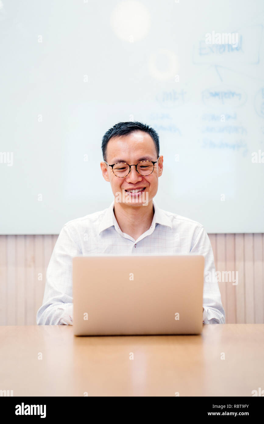 A young Chinese Asian business man is working on his laptop computer in ...