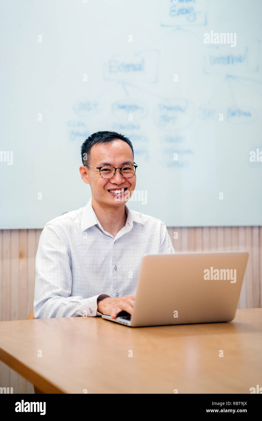 A young Chinese Asian business man is working on his laptop computer in ...