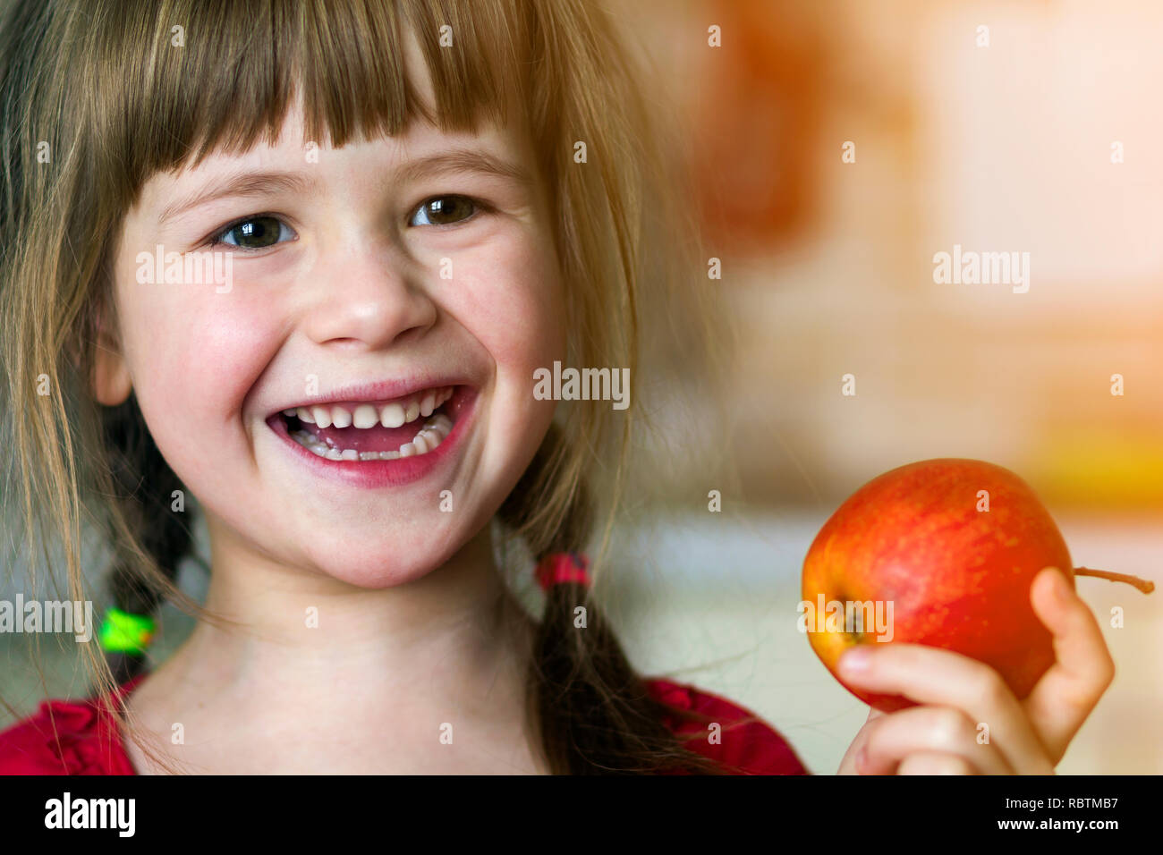 A cute little curly toothless girl smiles and holds a red apple ...