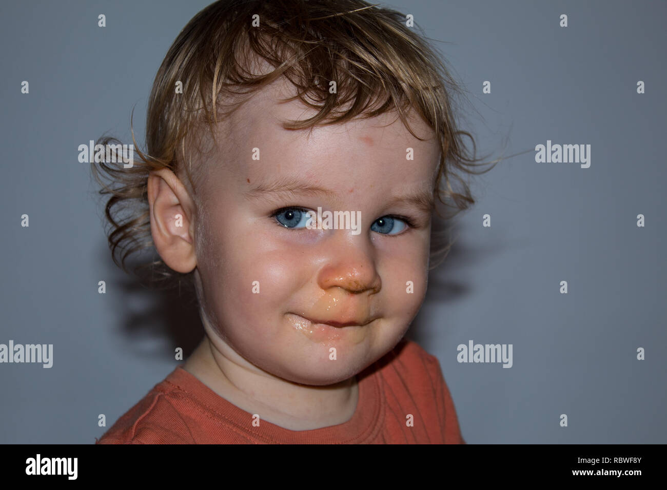 A portrait of a young boy with a runny nose isolated on grey background ...