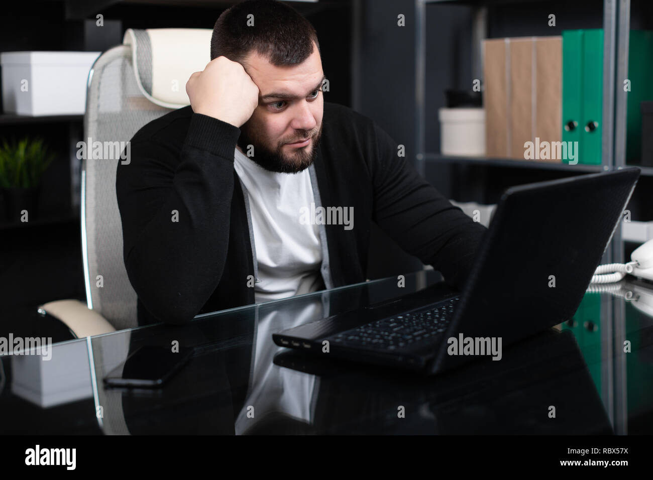 Portrait of young man propping up his head with his fist with laptop in ...