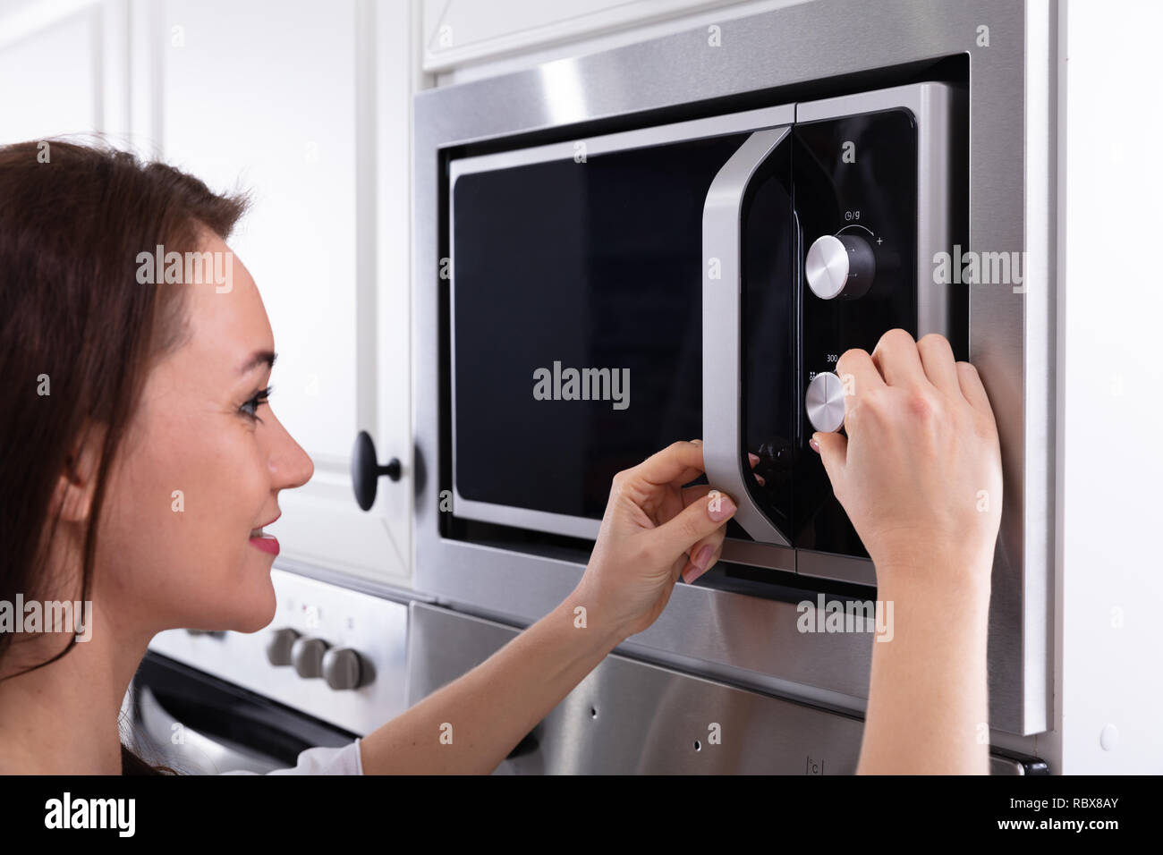Side View Of A Young Woman Using Microwave Oven In Kitchen Stock Photo ...