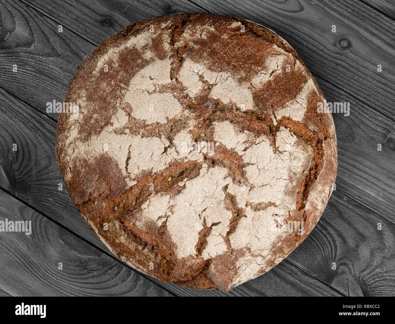 Round freshly baked round loaf of brown bread. Top view on lack wooden ...