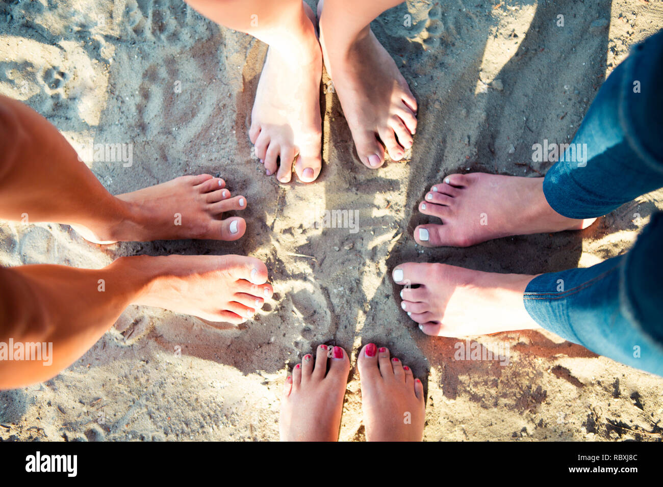 Top view image of feet of the female friends standing on the sand beach ...