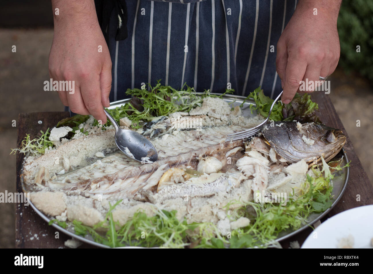 Chef in English restaurant serving prepared large fish on platter with ...