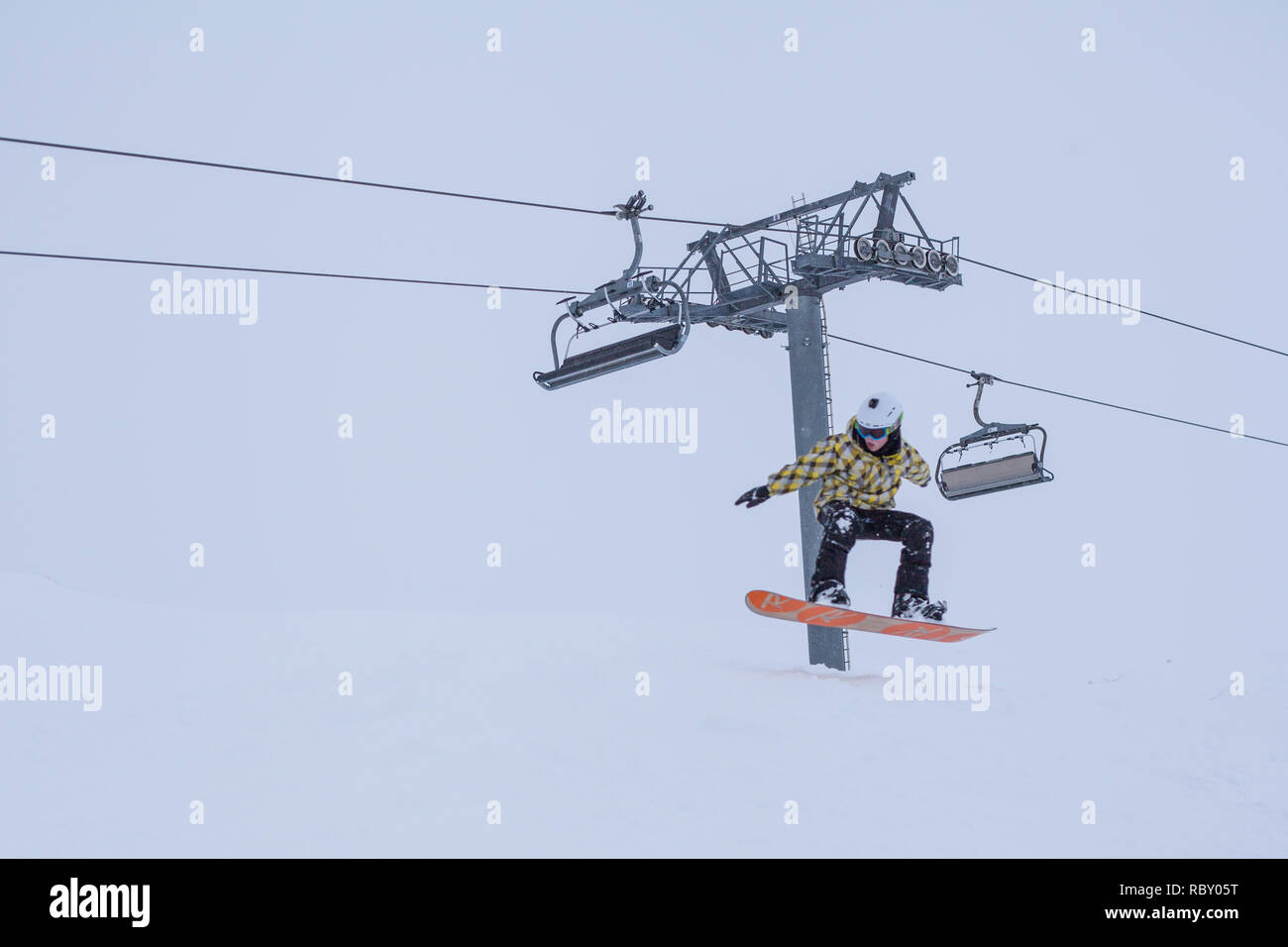 Snowboarding boy leaping into air while boarding down the slopes in the ...