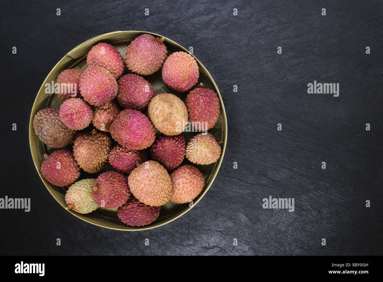 Lychees fruits in round bamboo bowl on black stone background surface ...