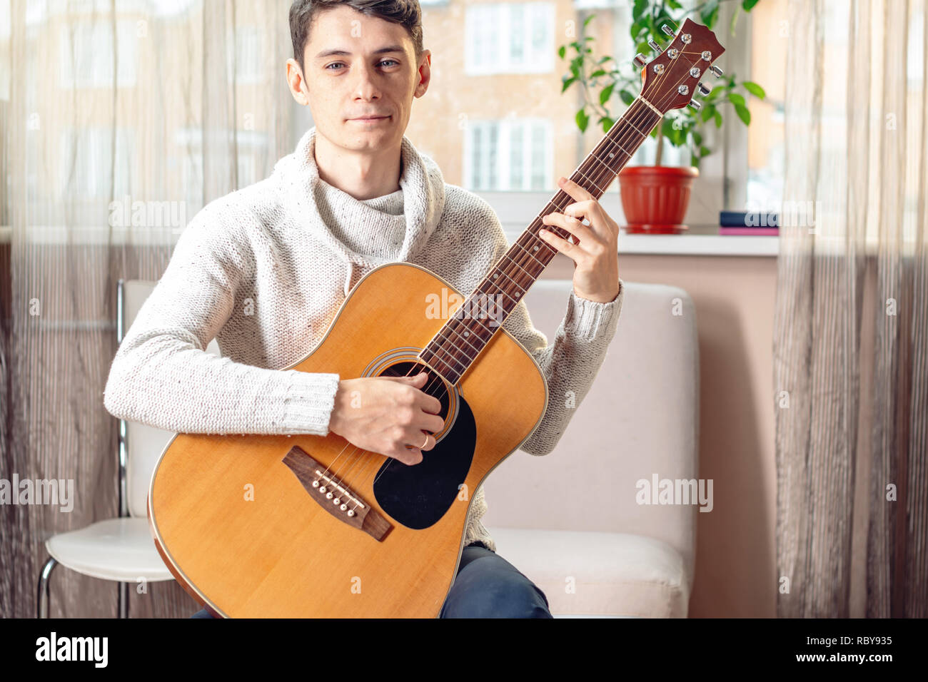Young attractive male musician sitting on a chair playing acoustic ...