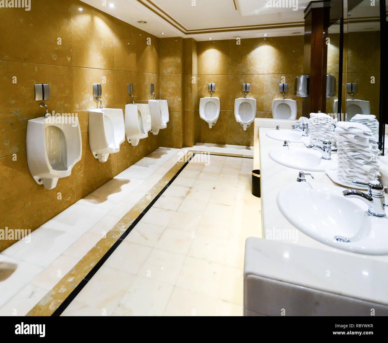 A row of urinals in tiled wall in a public luxurious restroom with sink ...