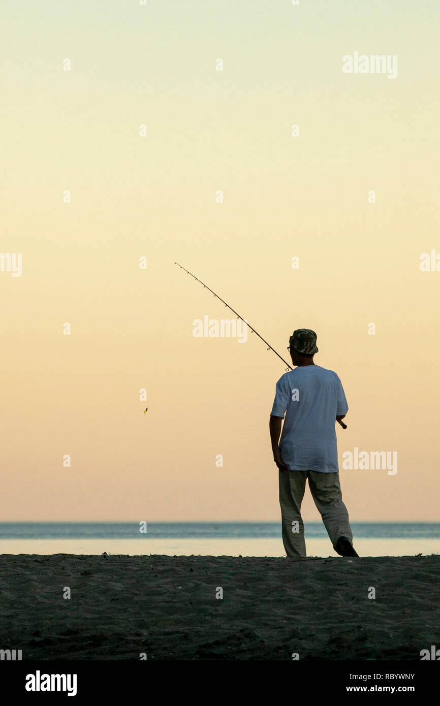 Stock Image One fisherman fishing from the beach at sunset on Lake ...