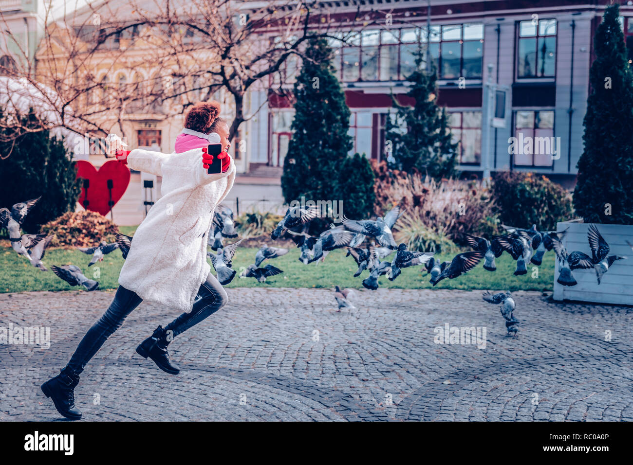 Happy brunette female running after street birds Stock Photo - Alamy