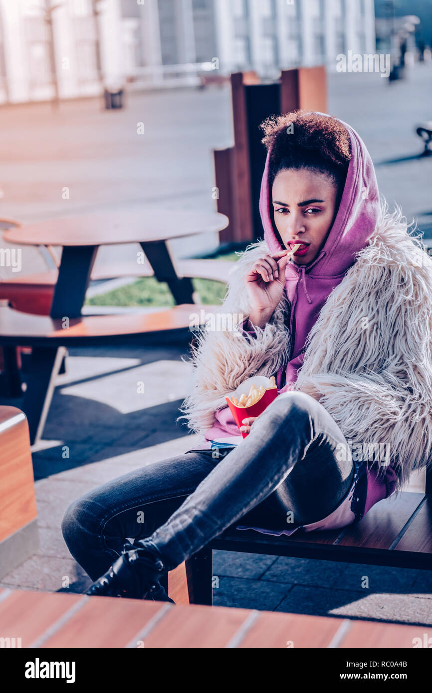 Hungry female person eating fries with pleasure Stock Photo - Alamy