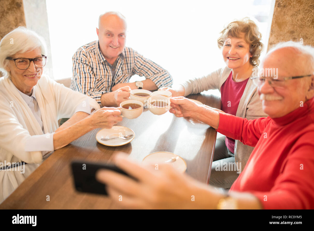 Cheerful seniors photographing together while drinking tea Stock Photo ...