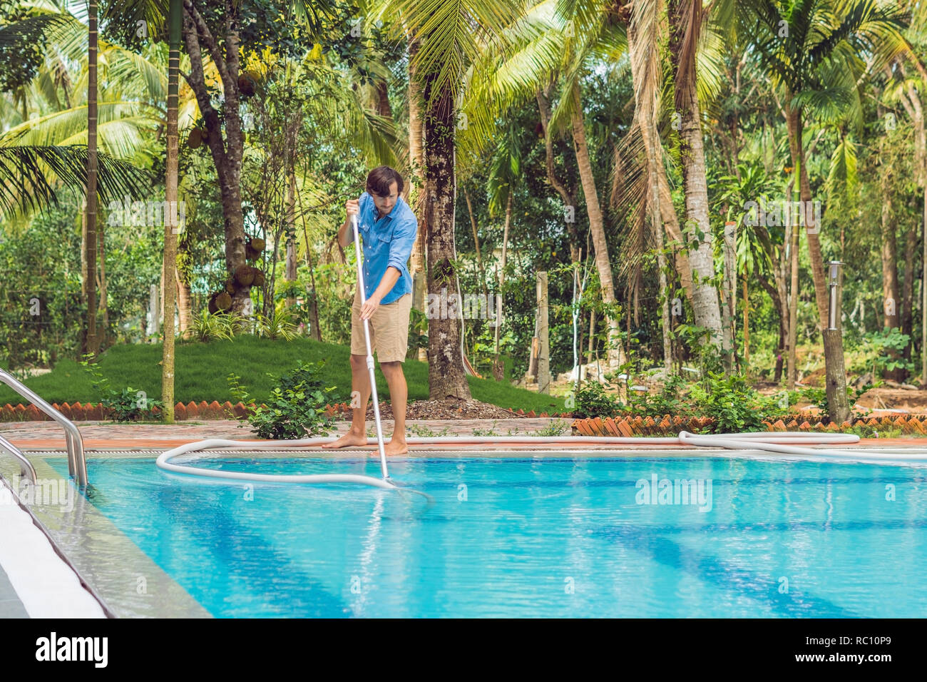 Cleaner of the swimming pool . Man in a blue shirt with cleaning ...