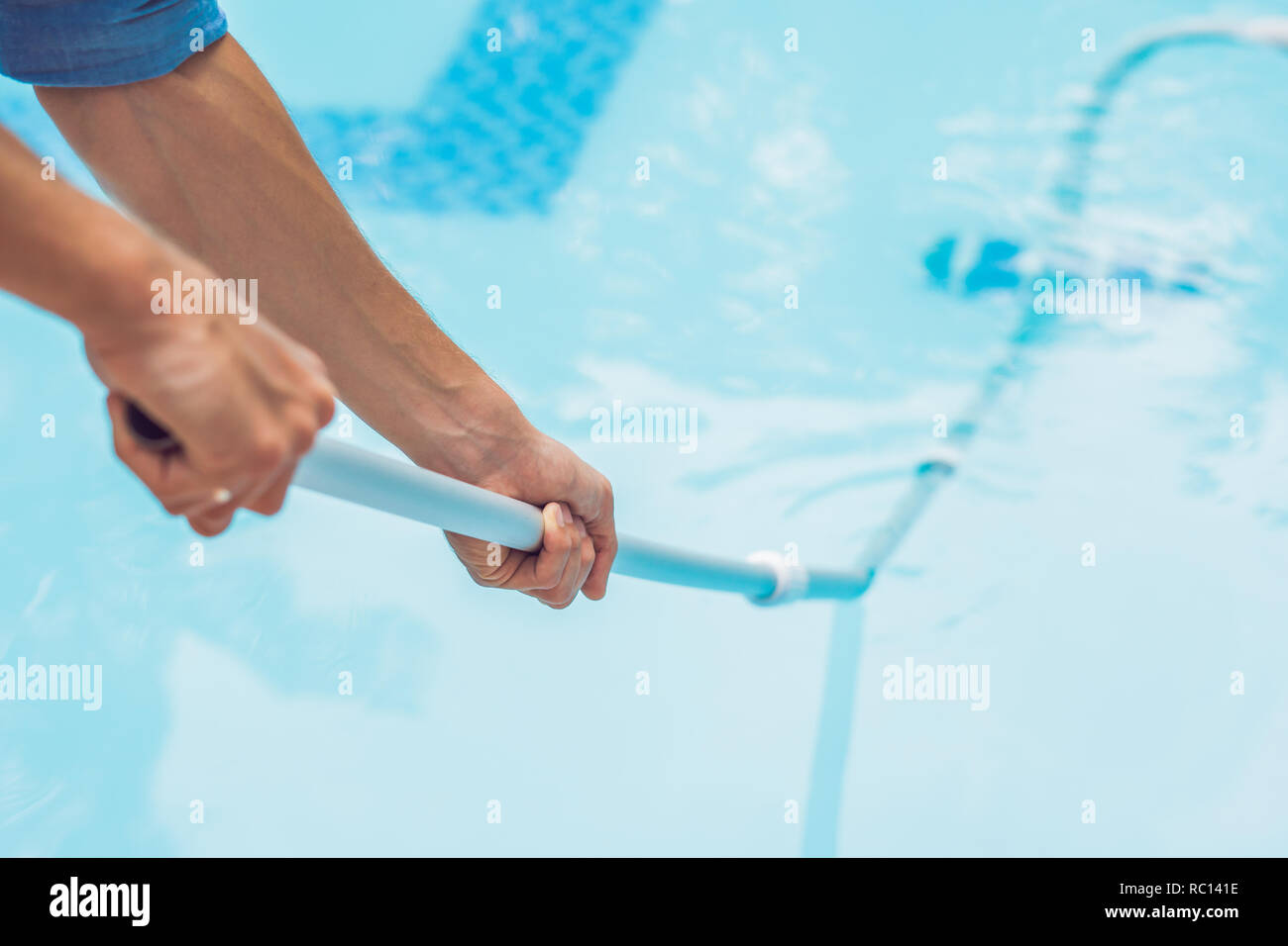Cleaner of the swimming pool . Man in a blue shirt with cleaning ...