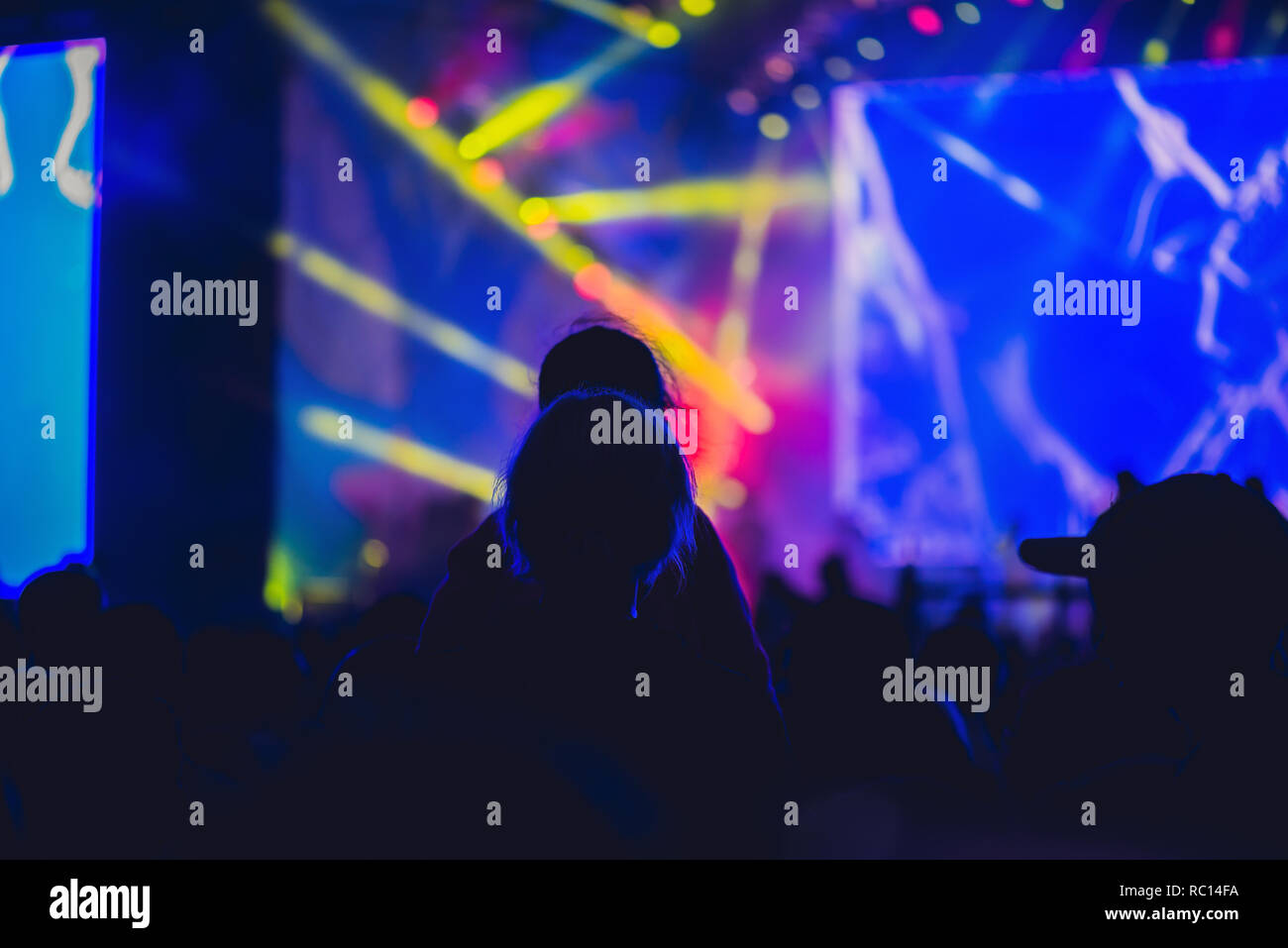 Silhouette of a big crowd at concert against a brightly lit stage ...
