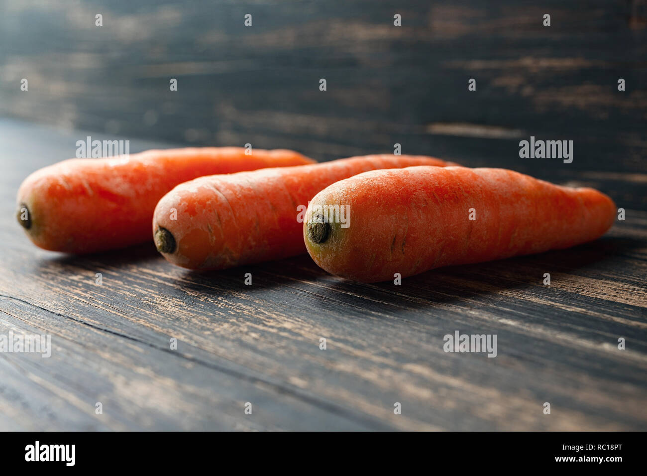 Three carrots on a dark rustic wooden background Stock Photo - Alamy