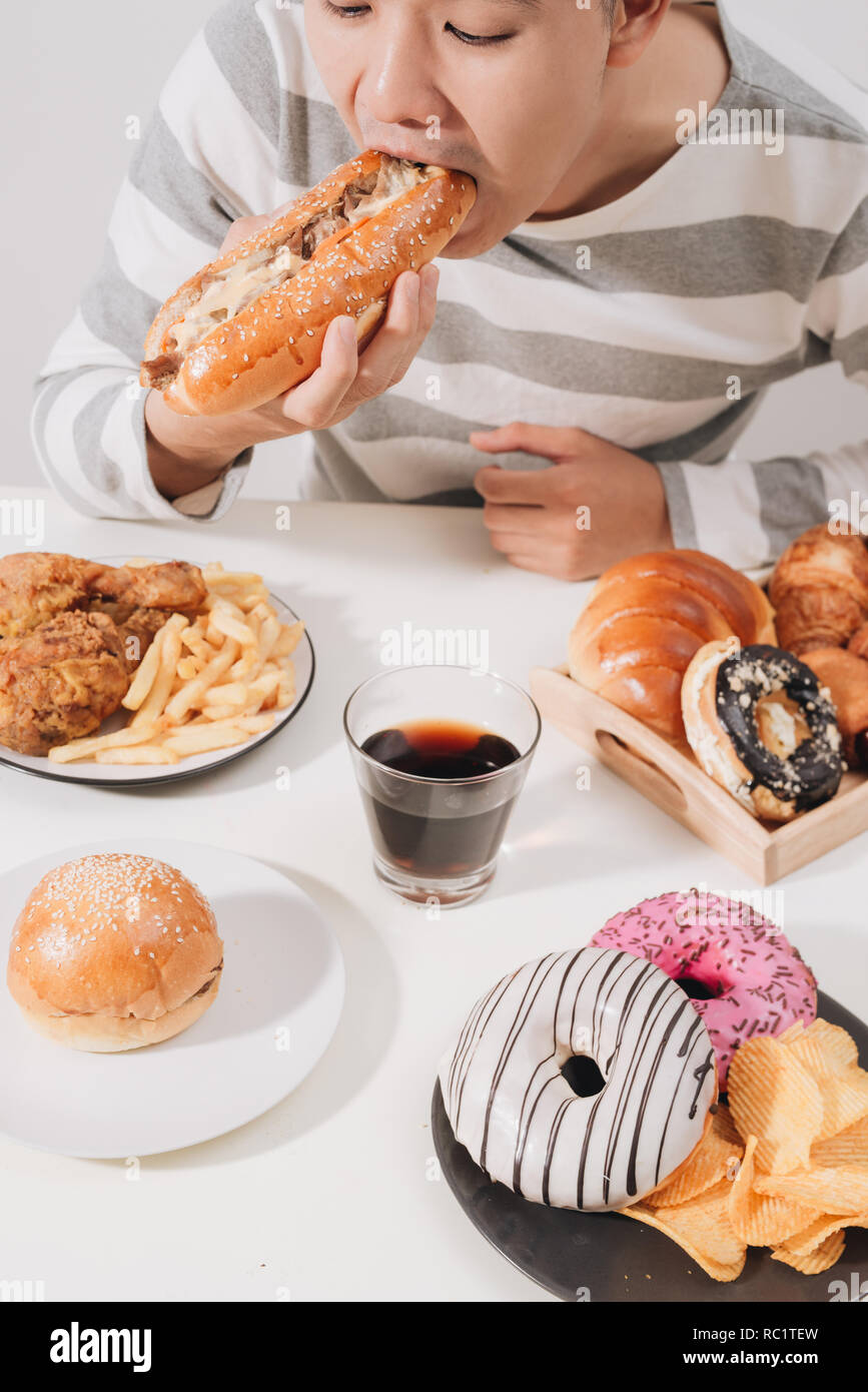 Portrait of asian man sitting and snacking donuts isolated over white ...