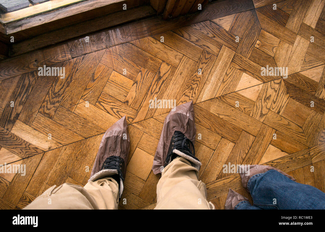 Overhead shot of human feet wearing overshoes standing on parquet floor ...