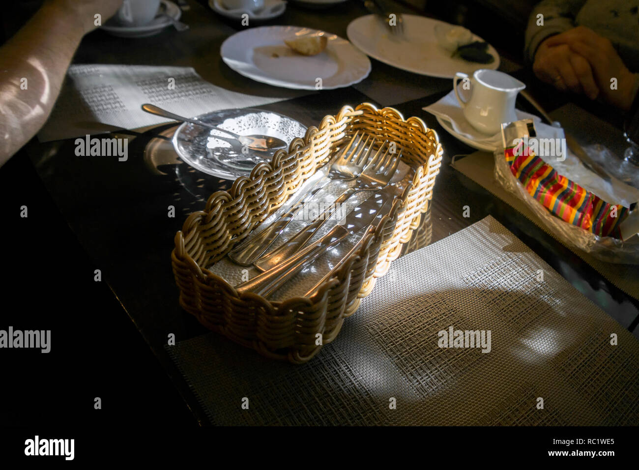 People eating at the messy table, a wicker basket with silverware in ...